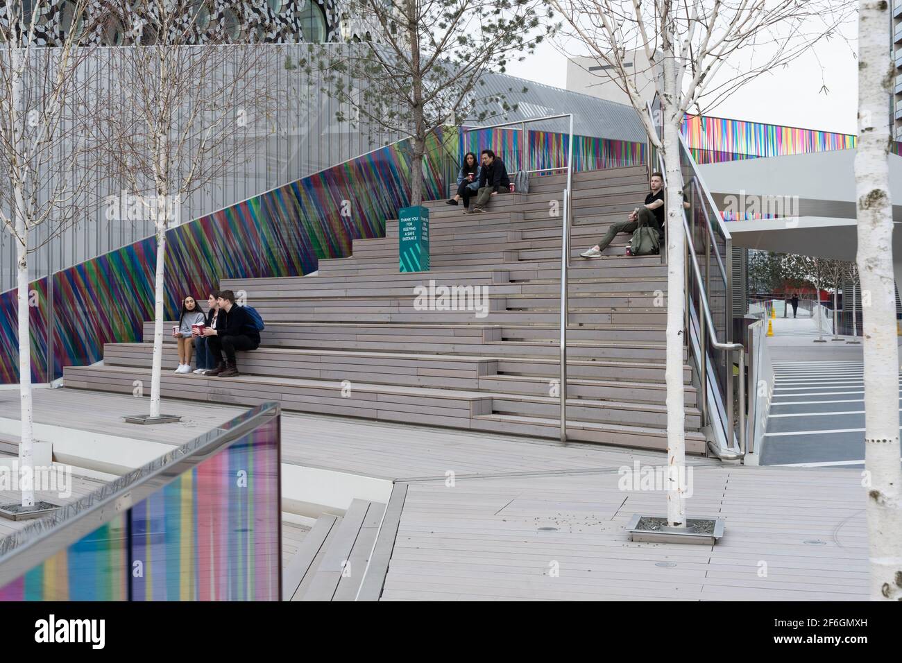 people sit on the steps of high walk in Greenwich Peninsula keeping ...