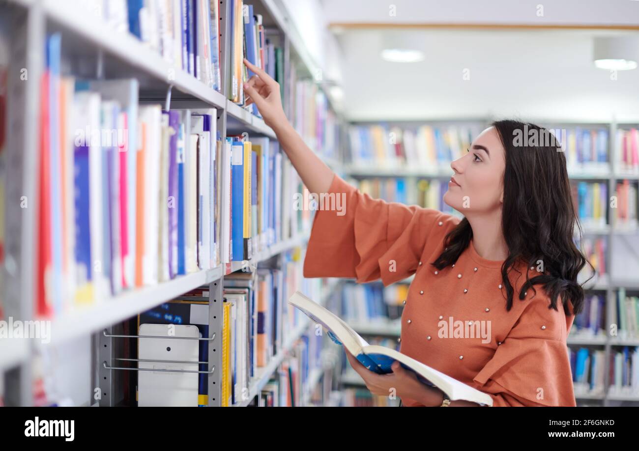 Reading a book in library. Young attractive librarian reading a book ...