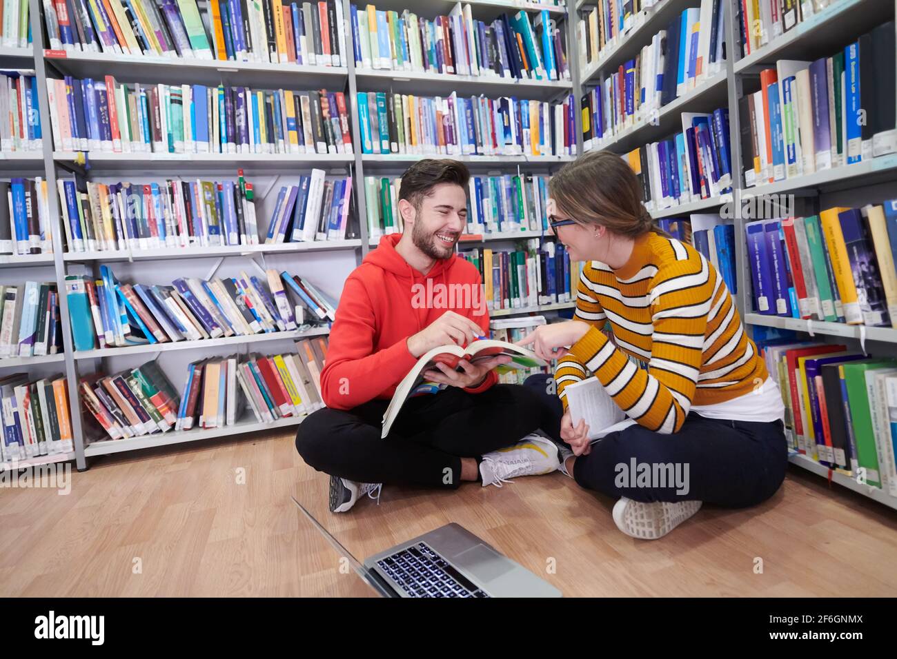 two young students sit in the school library and use a laptop to take ...