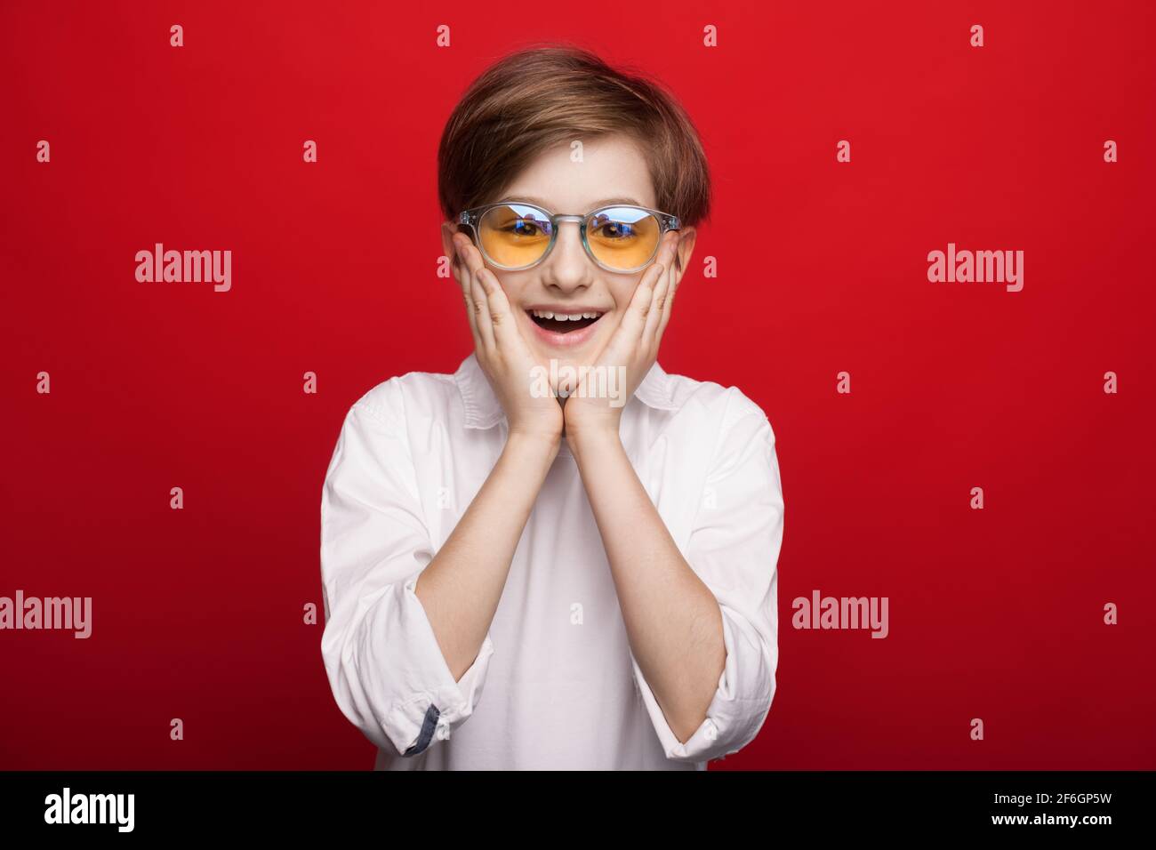 Small caucasian boy is surprised by something touching his cheeks and ...