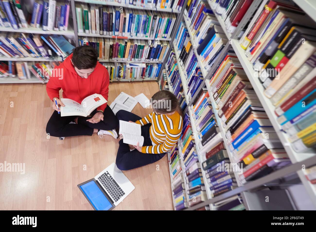 two young students sit in the school library and use a laptop to take ...