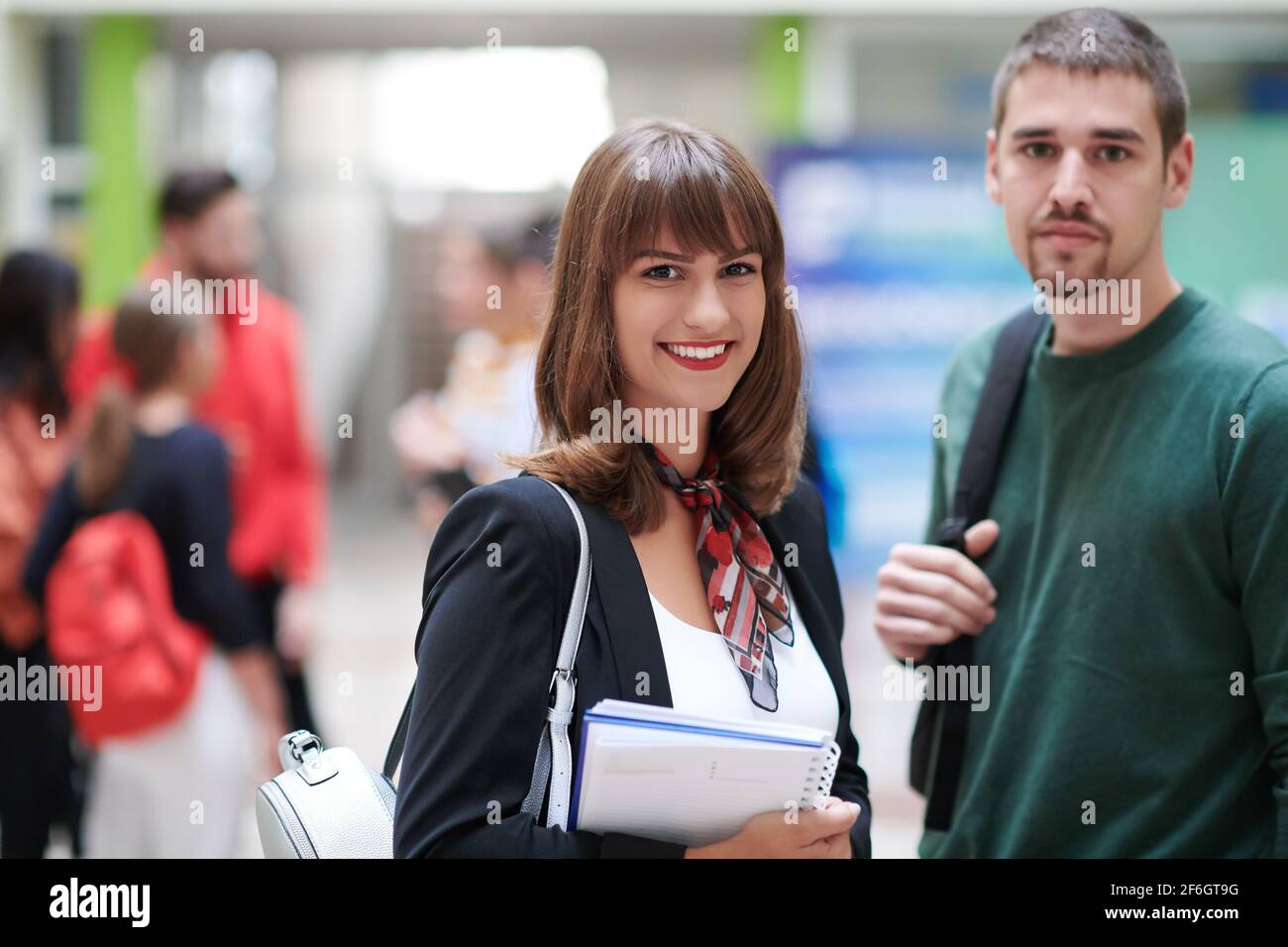 Two students using modern technology stand in the hallway while waiting ...