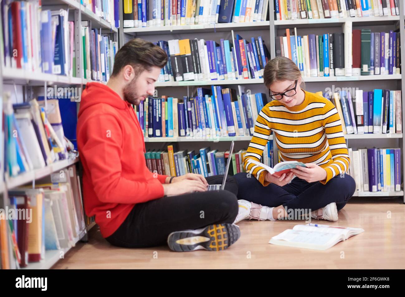 two young students sit in the school library and use a laptop to take ...