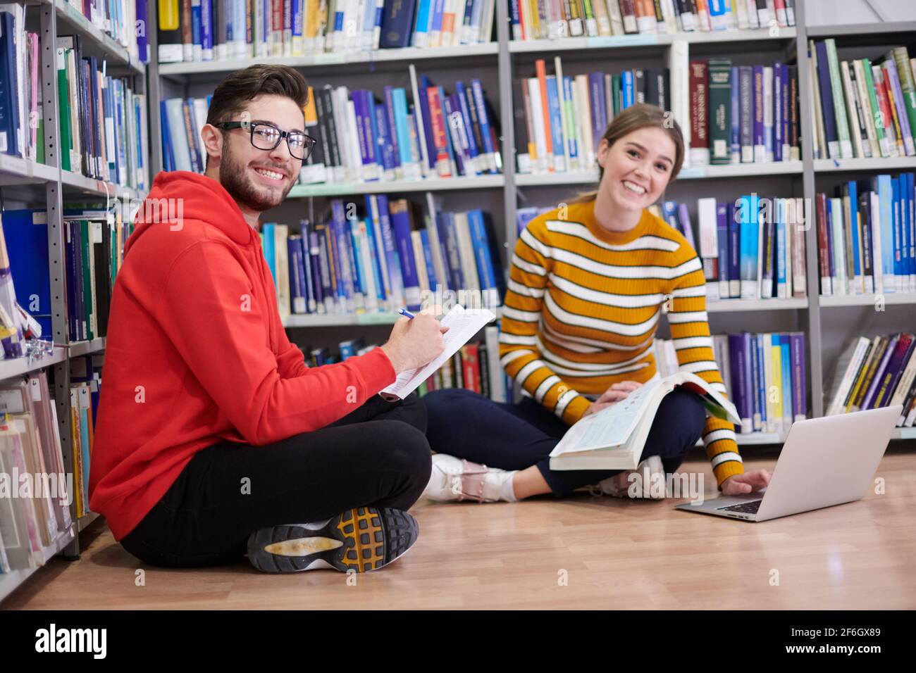 two young students sit in the school library and use a laptop to take ...