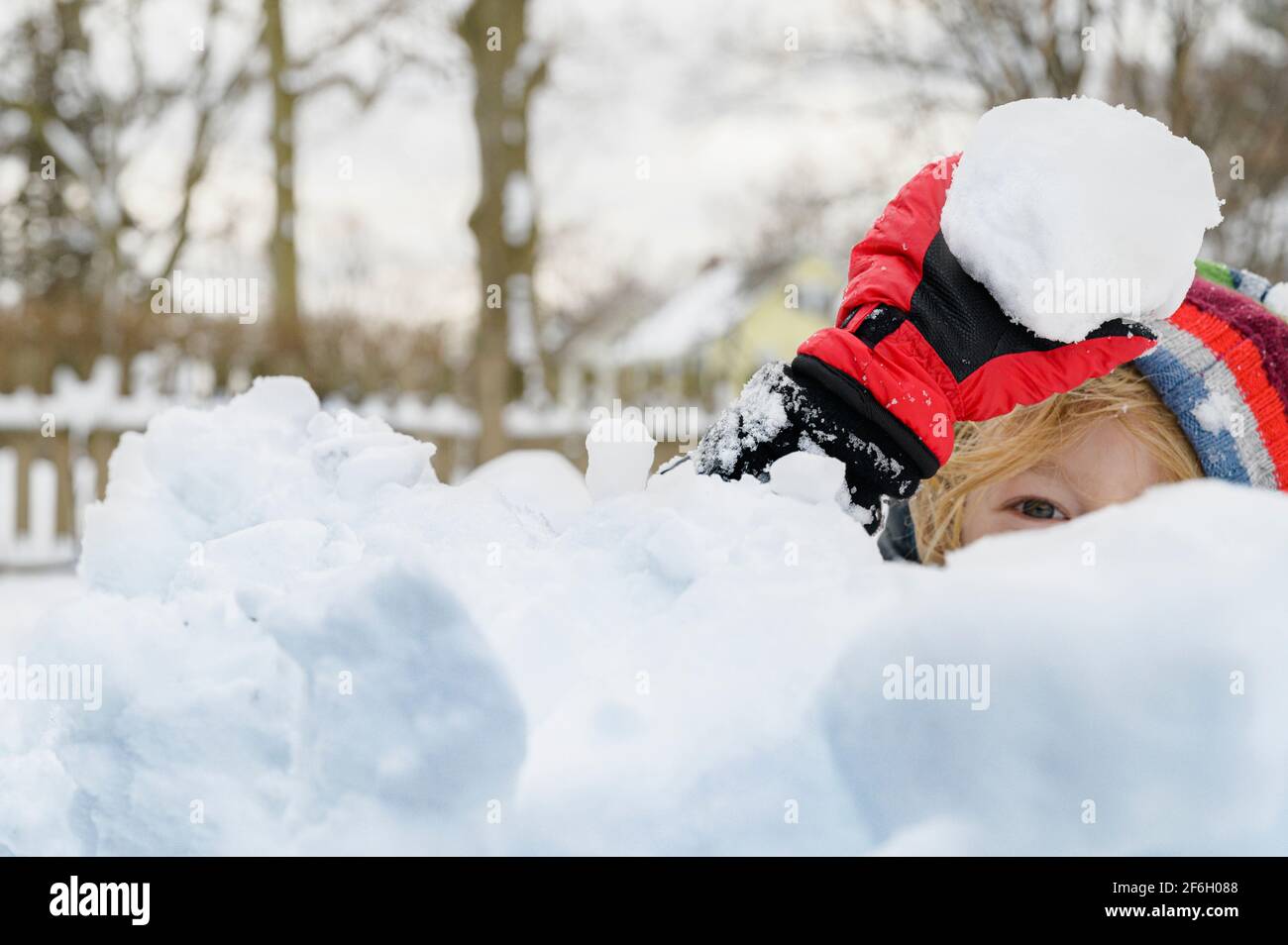 Boy (6-7) hiding behind pile of snow and holding snowball Stock Photo ...