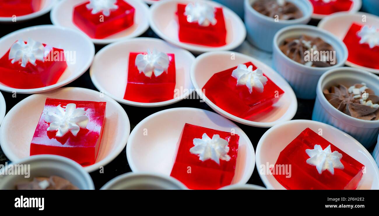 Red jelly dessert with whipped cream served on white plate. Square red ...