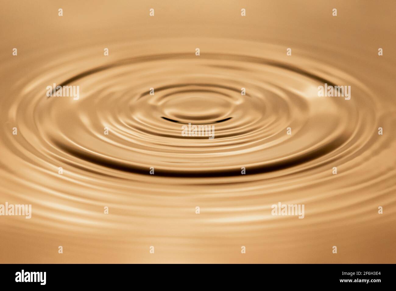 Water droplet dripping into golden pool creating ripples and abstract ...