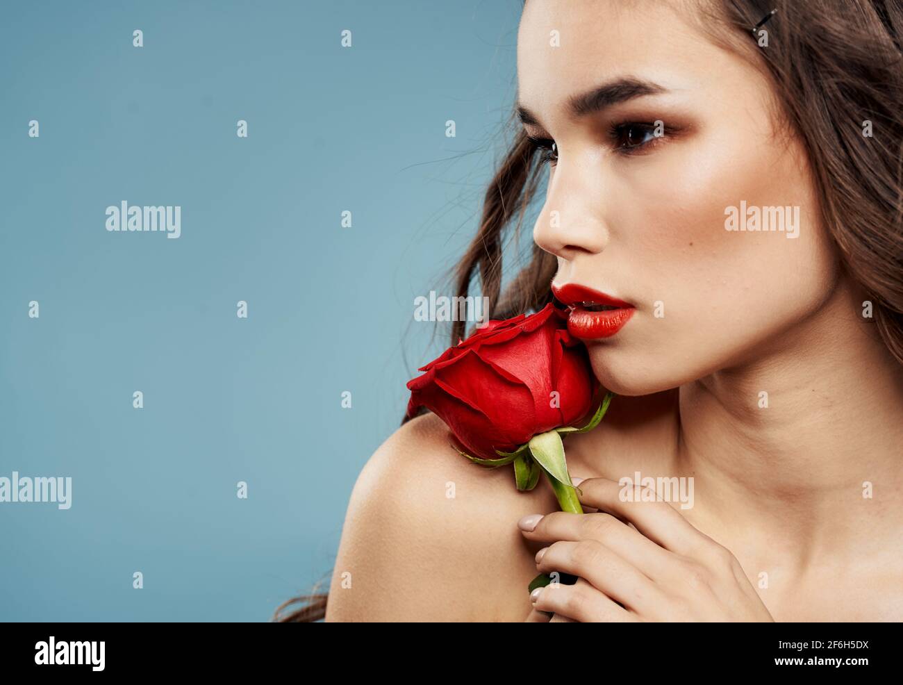 Young woman with red rose near face shadow on eyelids blue background ...