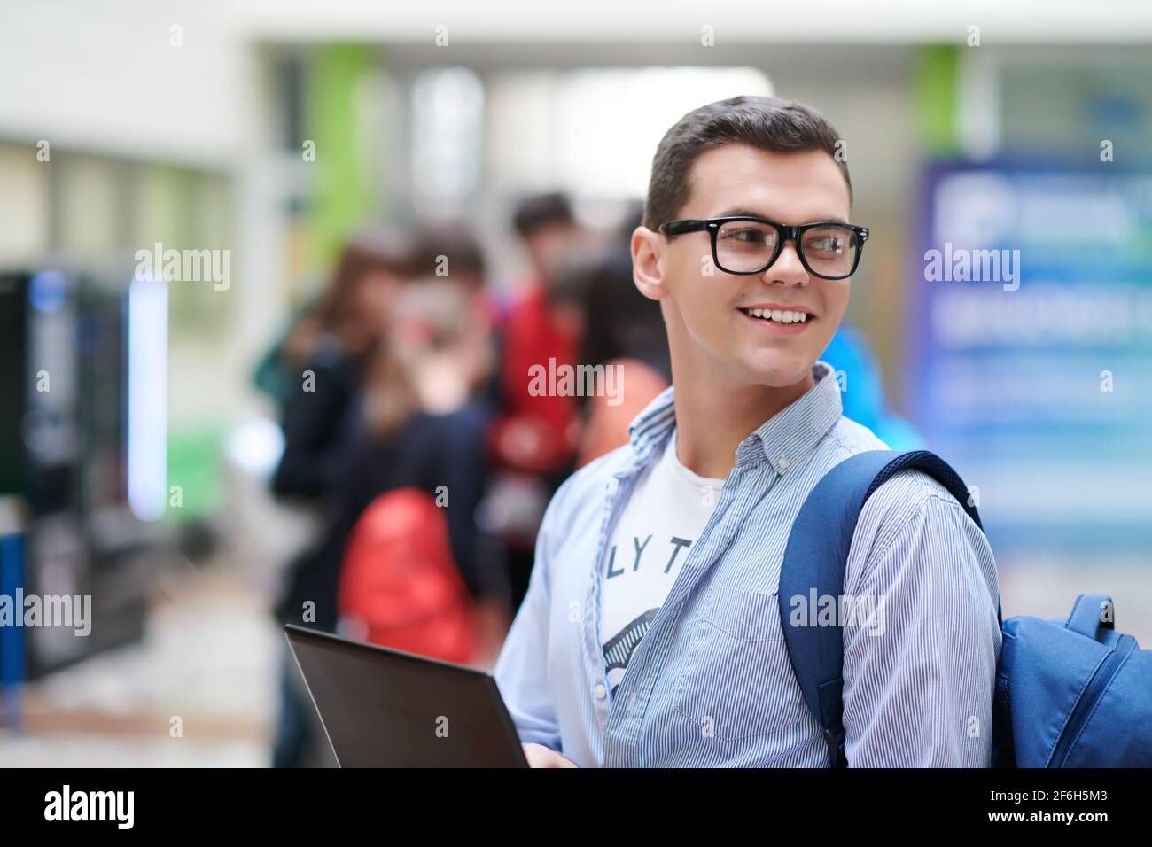 a student in glasses stands in the hallway of a modern college and uses ...