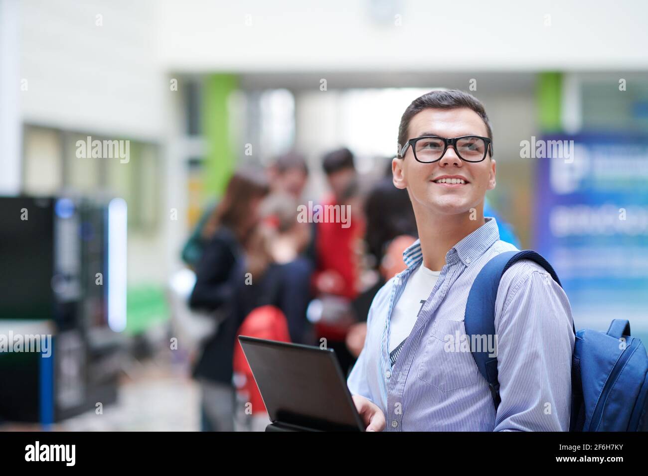 a student in glasses stands in the hallway of a modern college and uses ...
