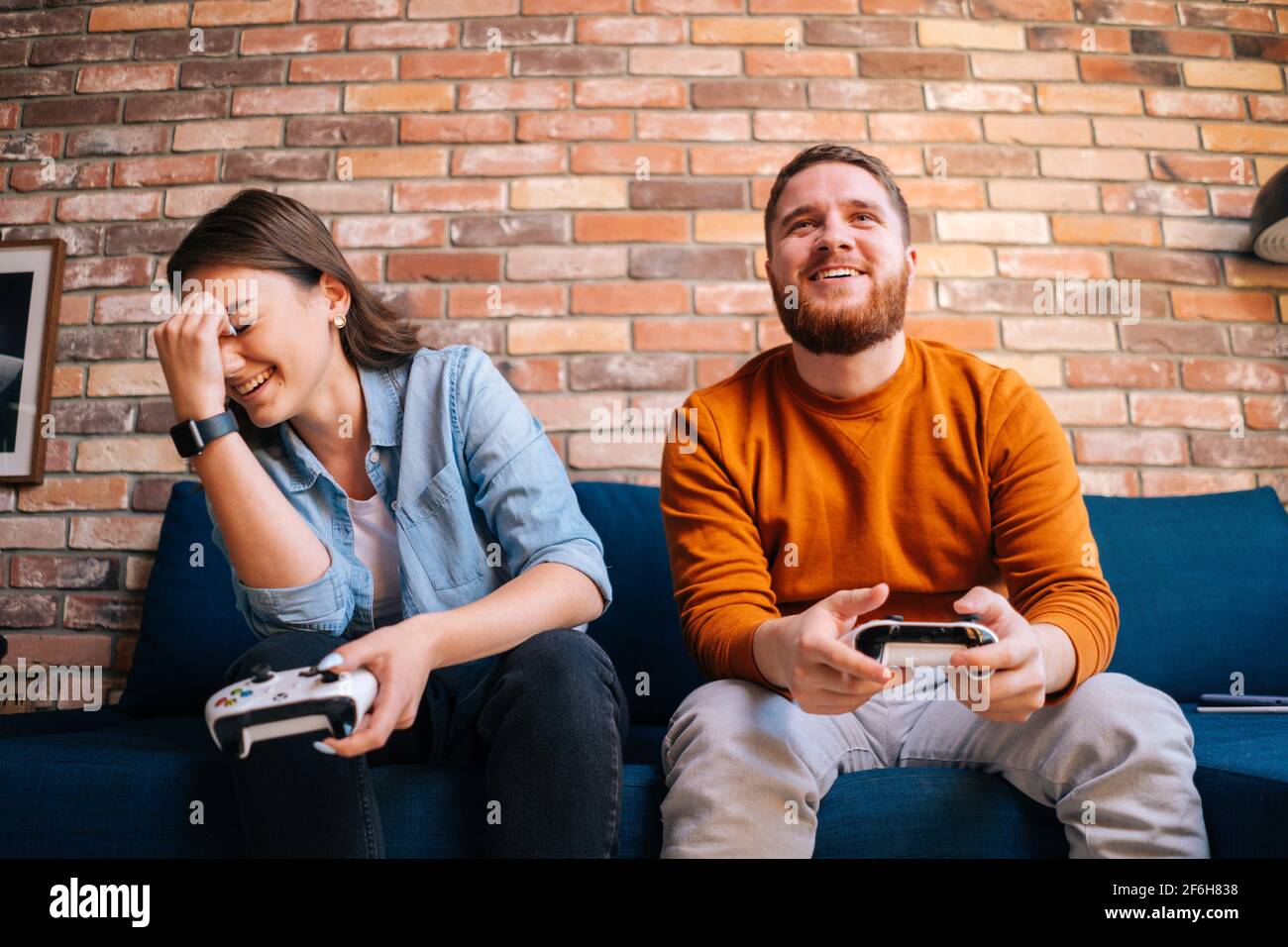 Front view of happy laughing young couple holding controllers and ...