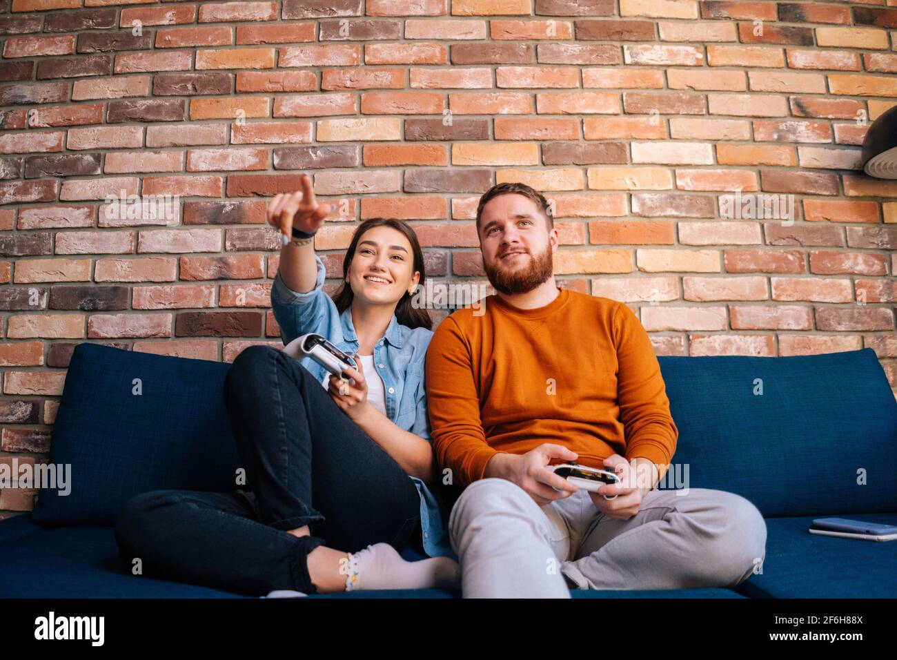 Portrait of happy cheerful young couple holding controllers and playing ...