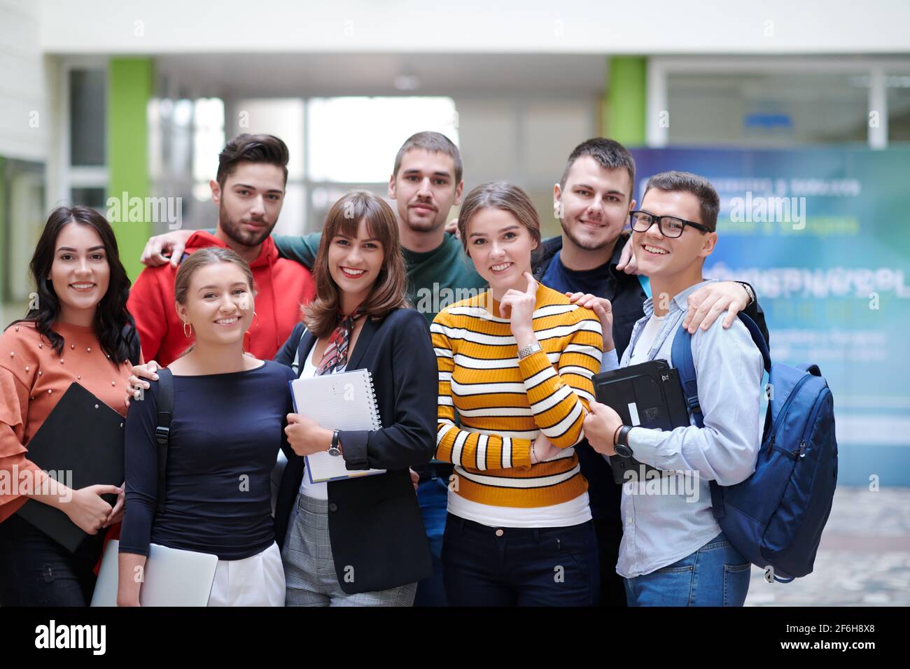 a group of students with books, a laptop and smartphones talk in a ...