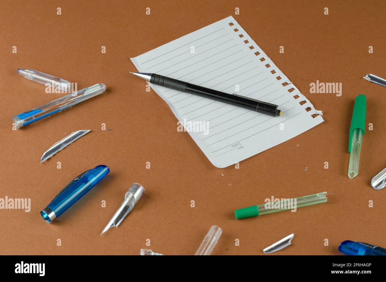 Broken pens and blank sheet of paper on brown table. Lots of random ...