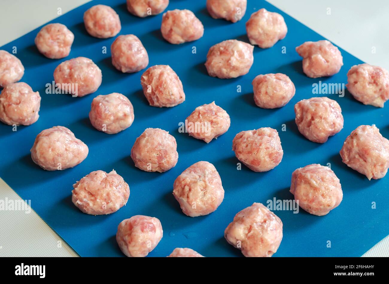 Raw shaped meatballs on blue. Rows of meatballs with pepper, salt and ...