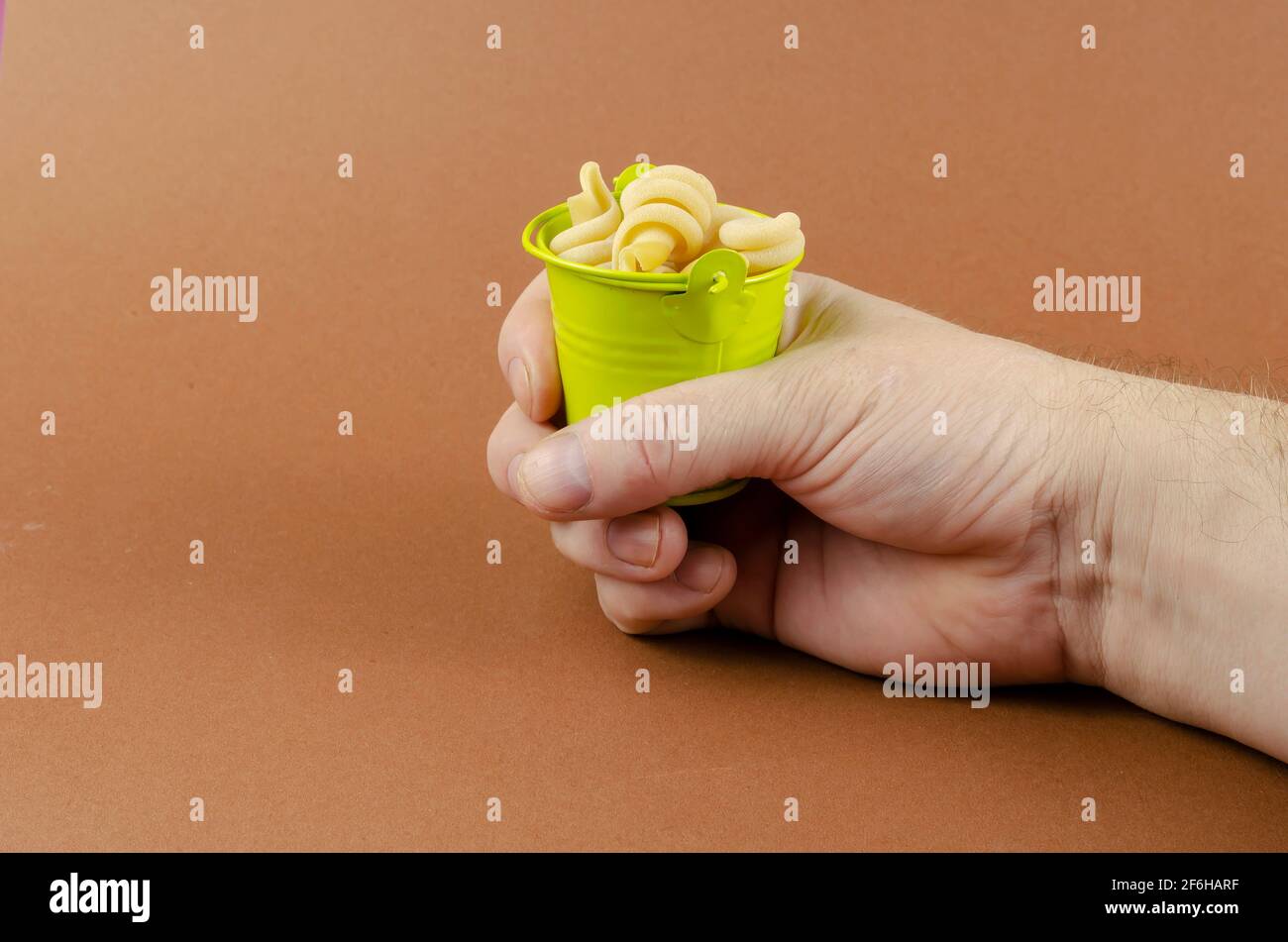 Green metal bucket, dry insalatonde pasta and hand on a brown ...