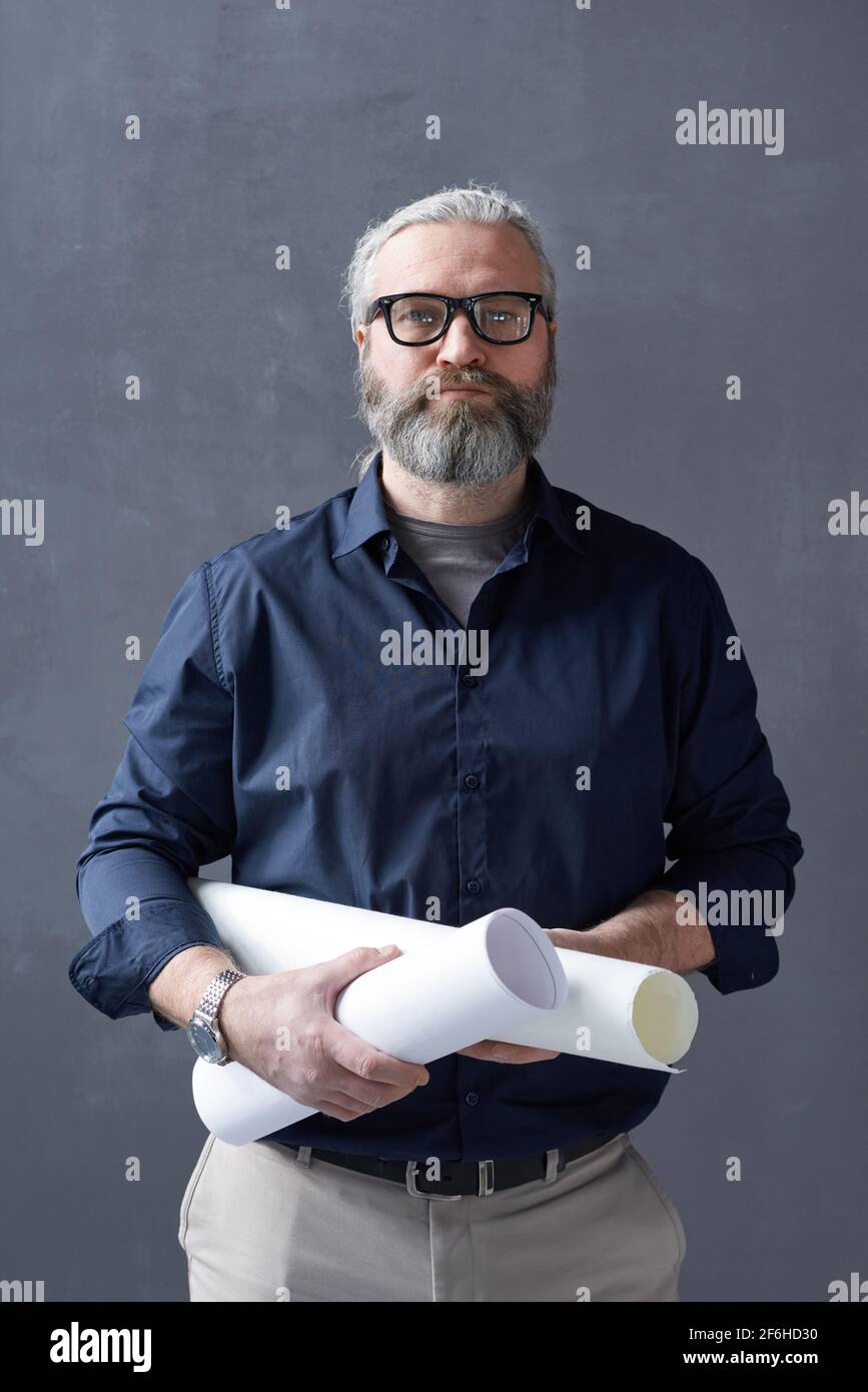 Portrait of mature bearded architect holding blueprint and looking at ...