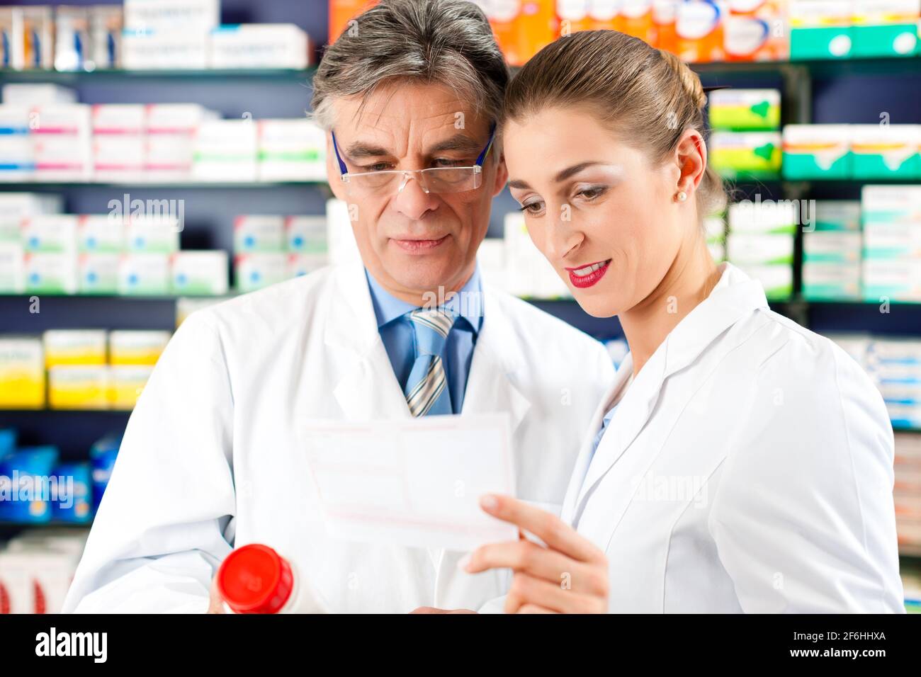 Two pharmacists with pharmaceuticals in hand consulting each other in a ...