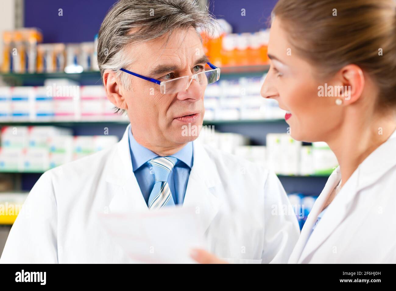 Two pharmacists with pharmaceuticals in hand consulting each other in a ...