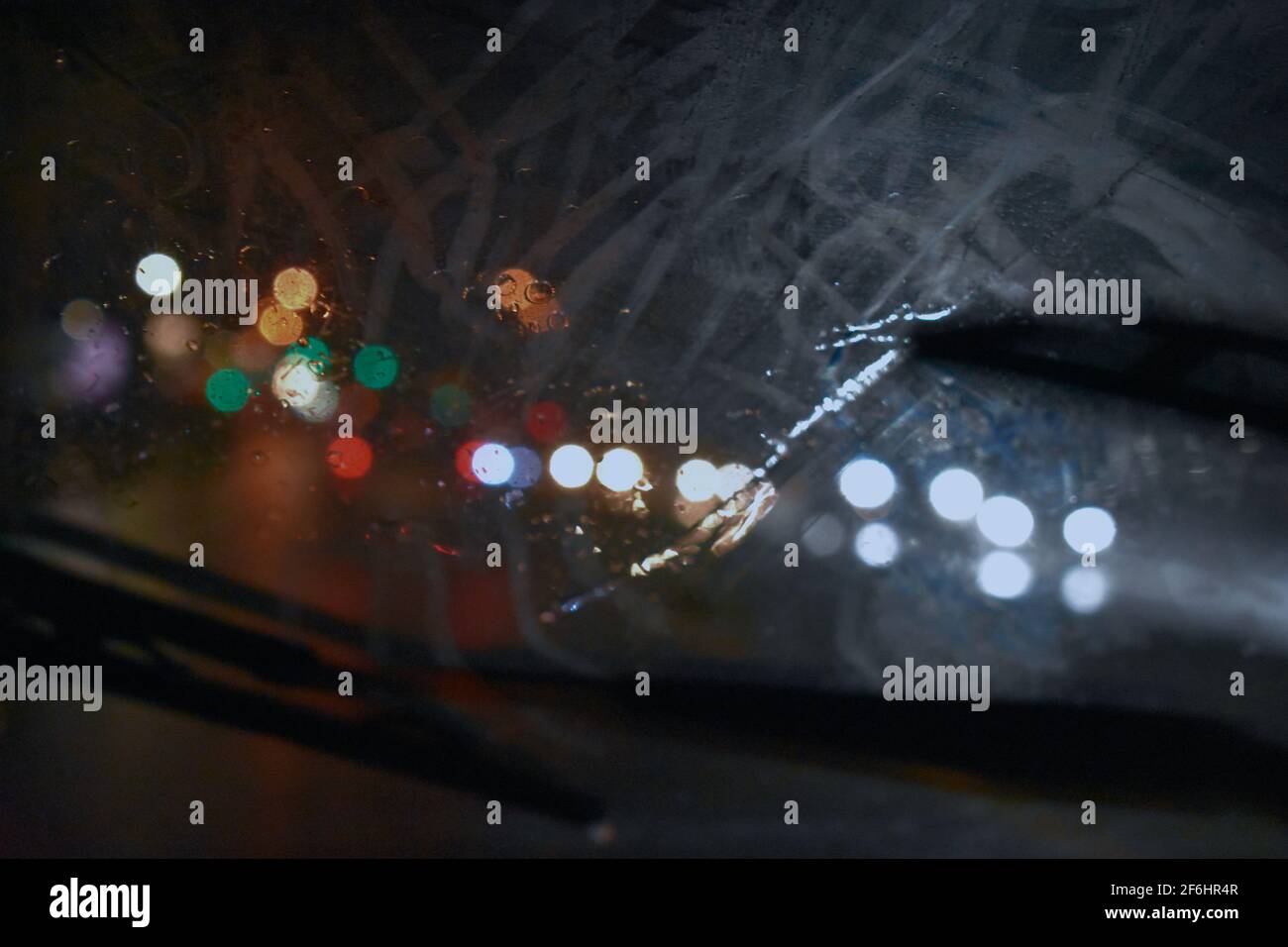 Windshield wipers on a windshield with headlights and traffic lights in ...