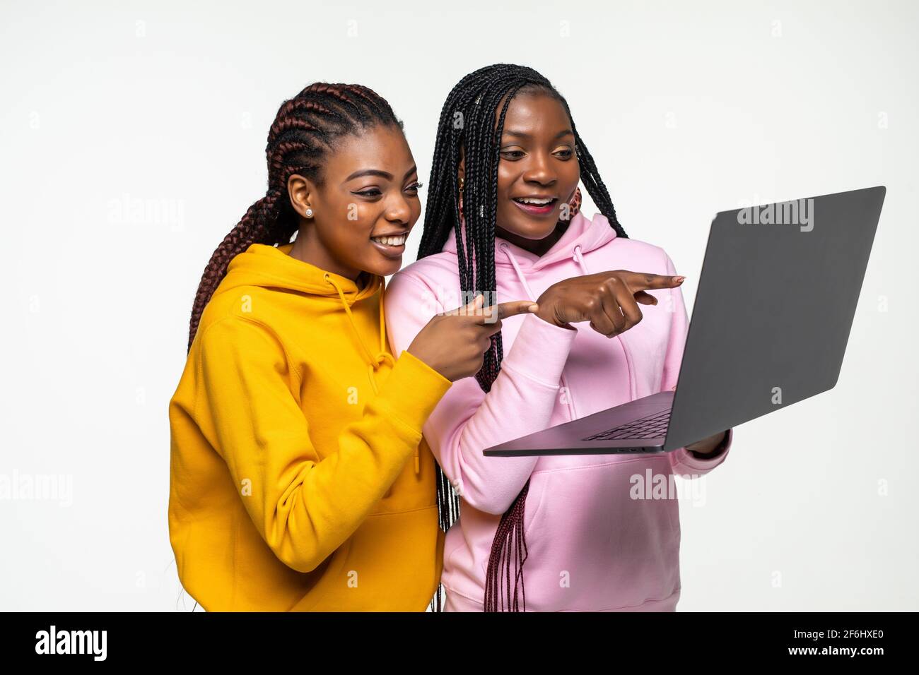 Two african young women standing holding and using a laptop on white ...