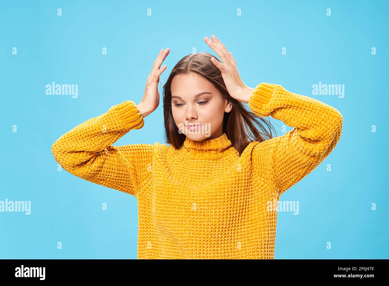 woman in yellow sweater holds hands near head emotions blue background ...