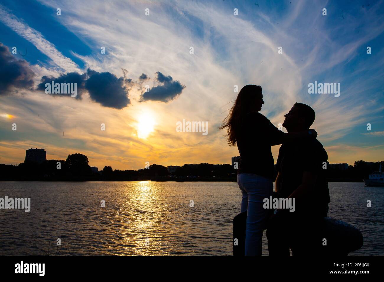 Silhouette of a loving couple cuddling during a golden sunset reflected ...