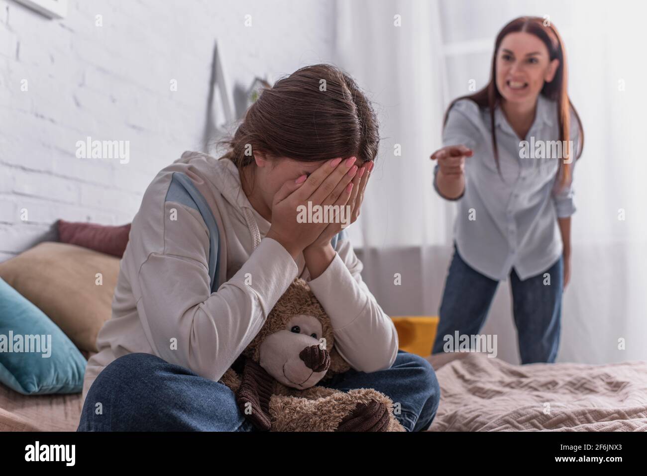 teenage girl covering face near angry mother on blurred background ...