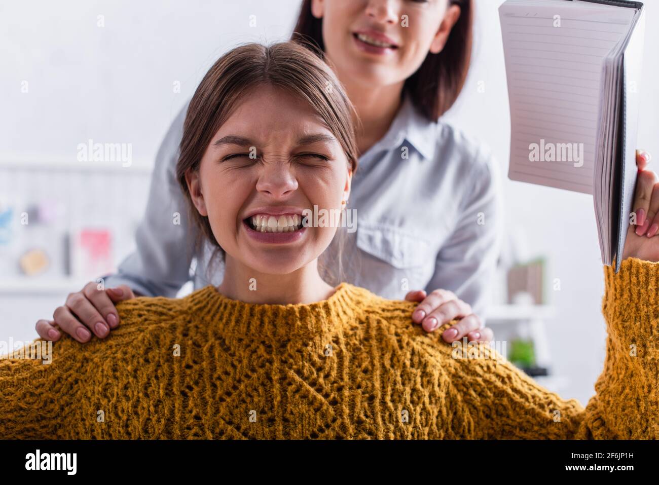 Angry Teenage Daughter Holding Notebook Near Worried Mother Stock Photo angry-teenage-daughter-holding-notebook-near-worried-mother-stock-photo