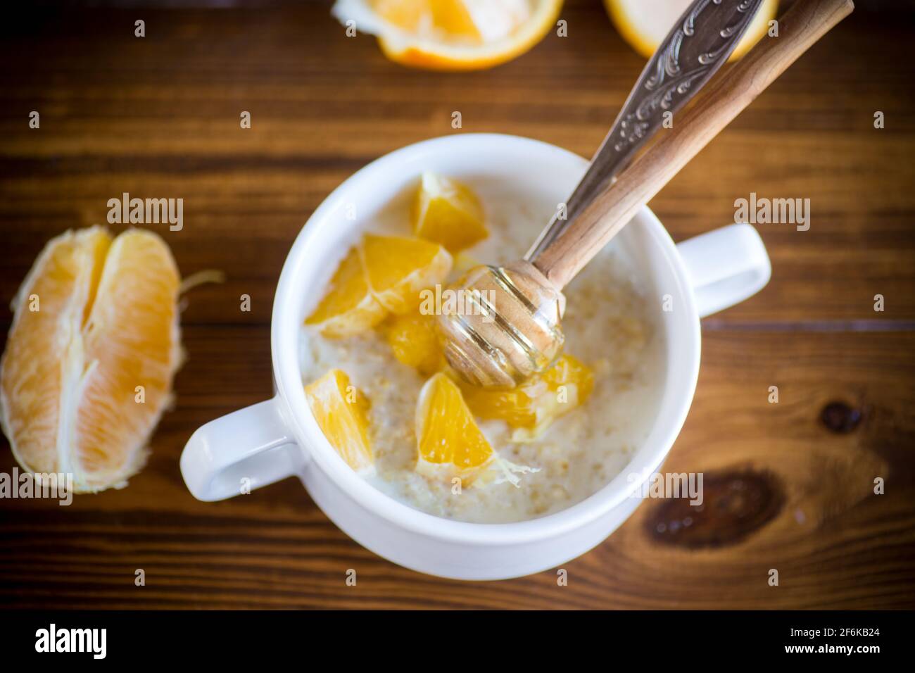 cooked boiled sweet oatmeal with oranges in a bowl on a wooden table ...