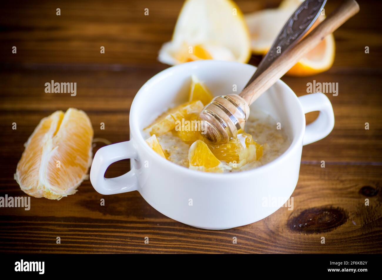 cooked boiled sweet oatmeal with oranges in a bowl on a wooden table ...