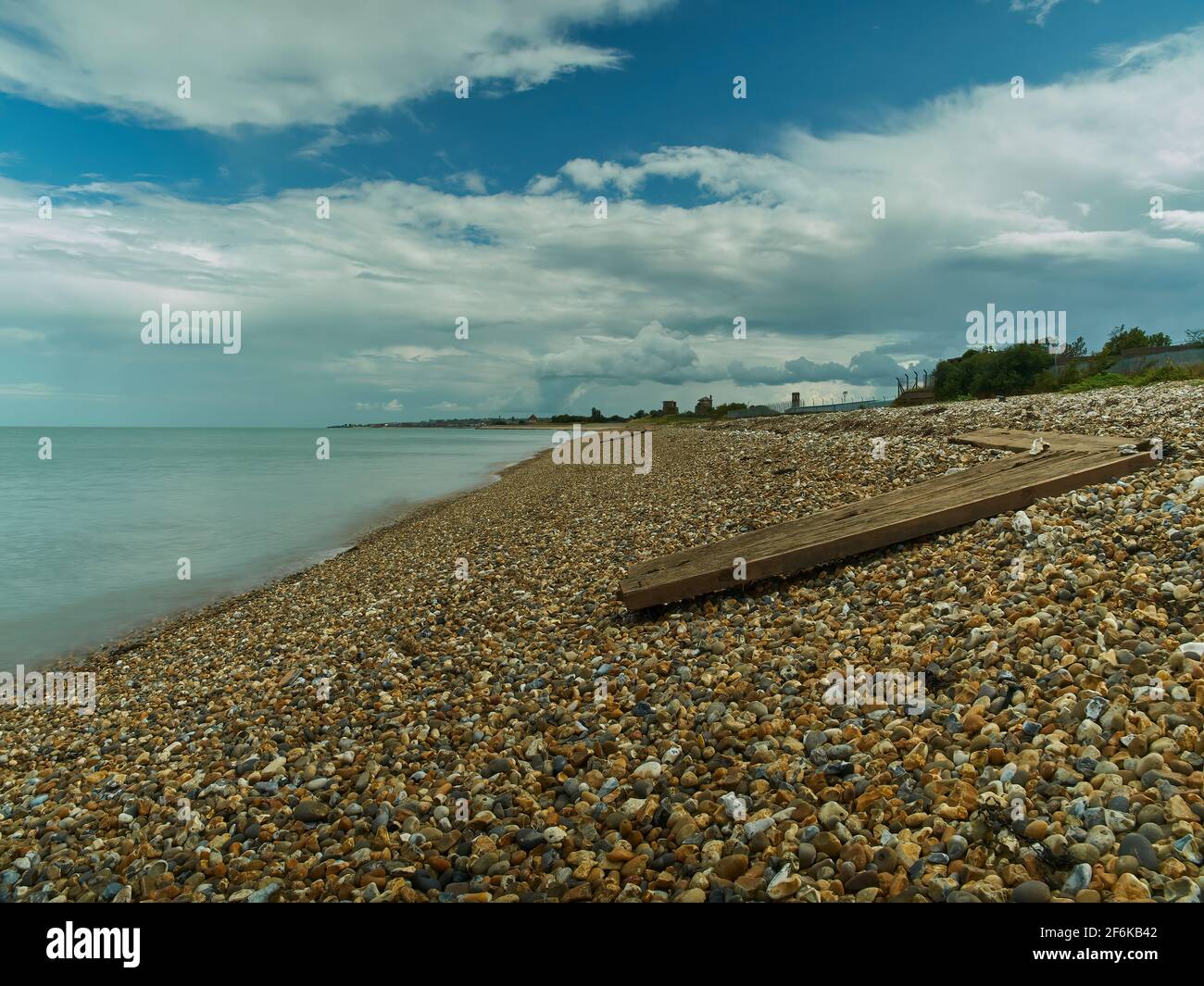Drift wood on a long sweep of shingle beach. Buildings spot the horizon ...