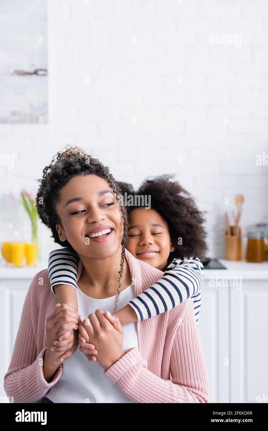 happy african american girl with closed eyes holding hands of cheerful mother in kitchen Stock ...