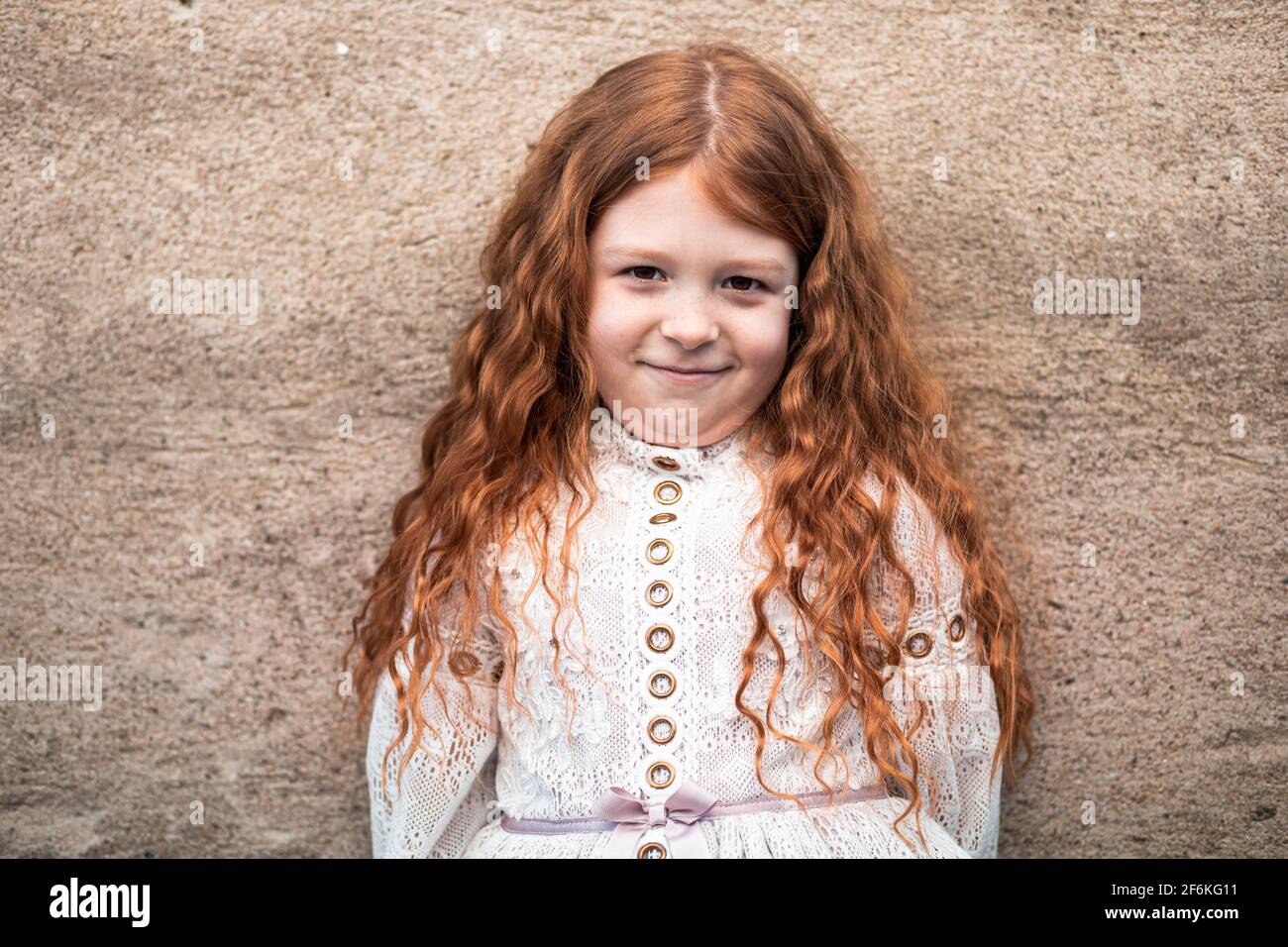 Portrait of a cute, little, ginger girl in white dress looking shy ...