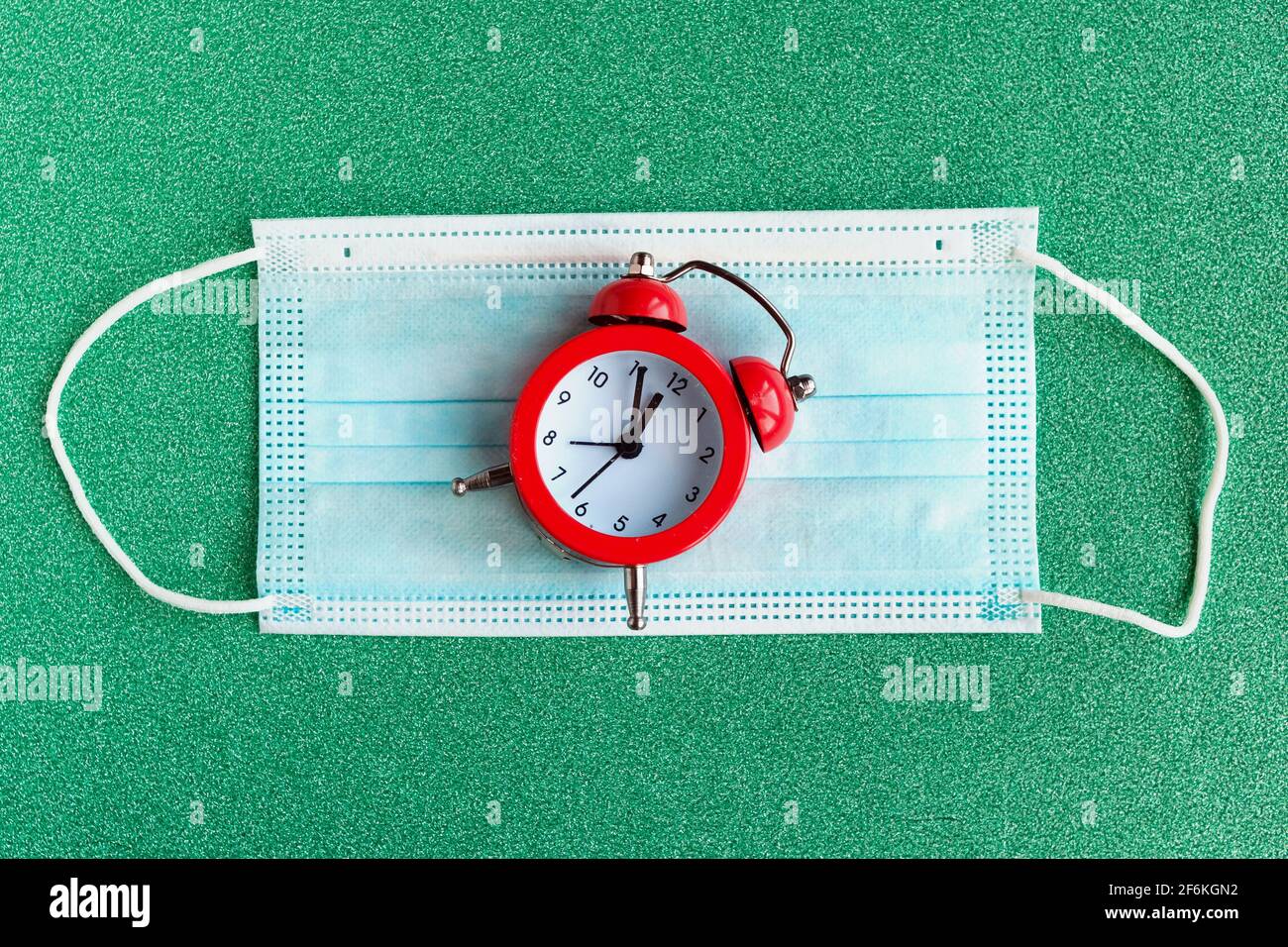 Alarm clock and face medical mask on green glitter background. Minimal ...
