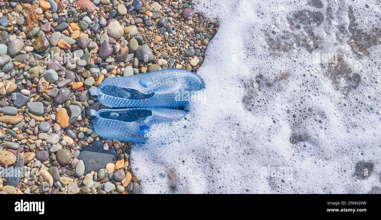 Rubber blue women's slippers for swimming on a pebble beach with sea ...