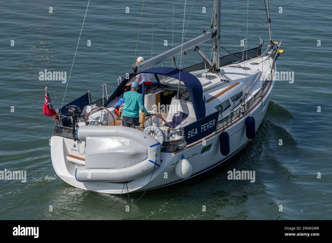 a man at the helm of a large racing or cruising yacht steering the boat ...