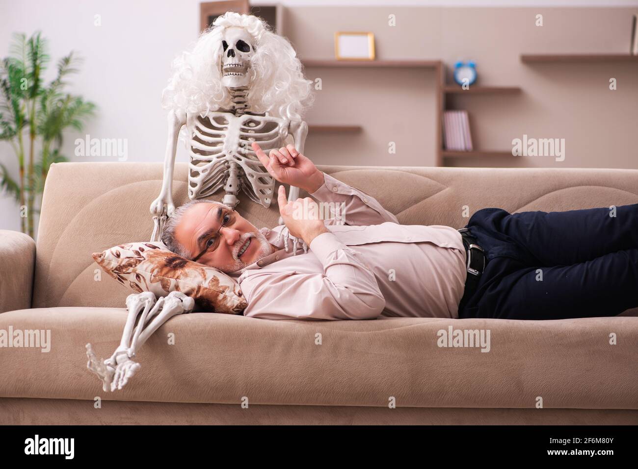 Old man sitting on the sofa with the female skeleton in undying love ...