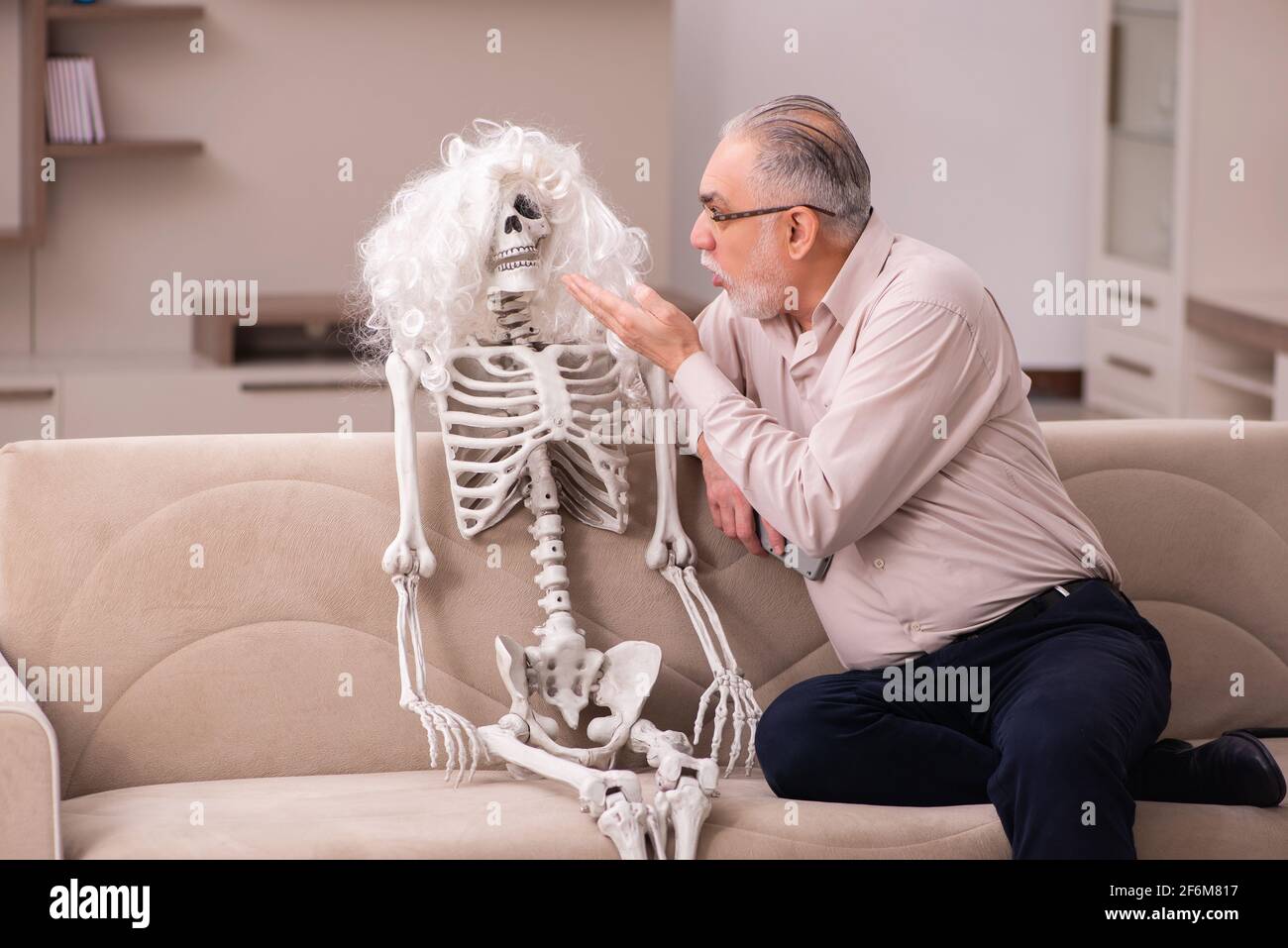 Old man sitting on the sofa with the female skeleton in undying love ...
