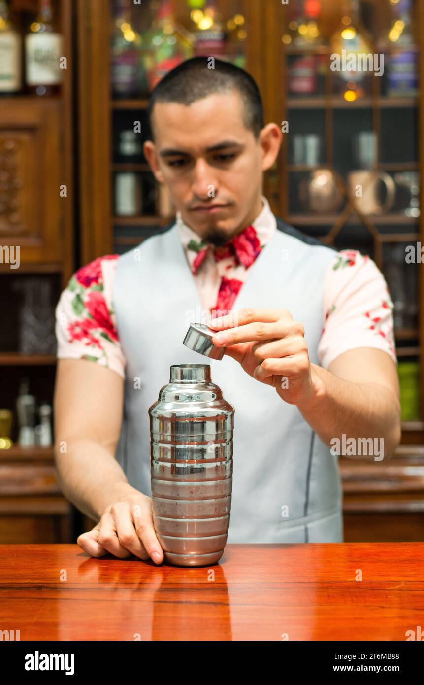Young handsome smiling barman in bar interior shaking and mixing ...