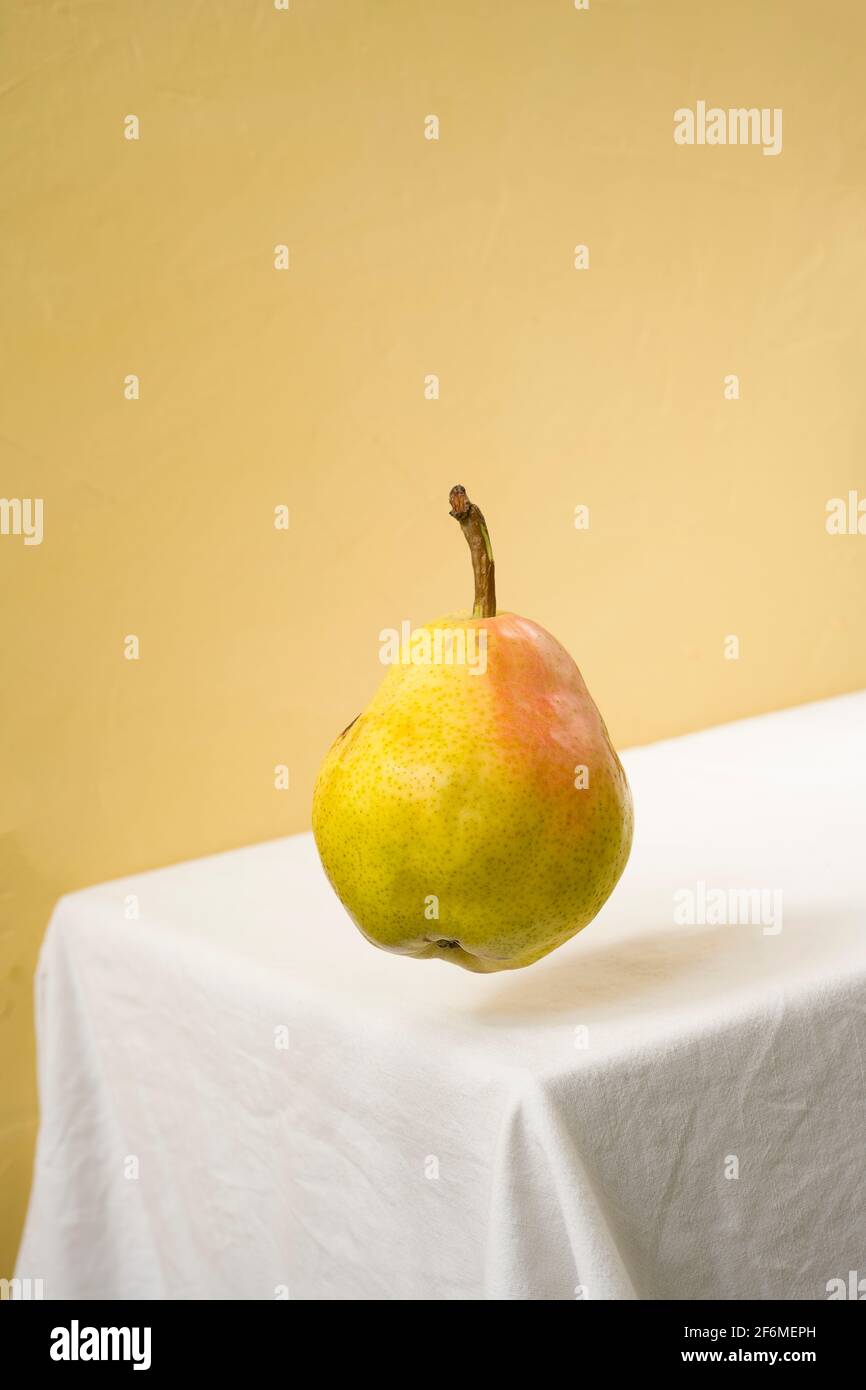 Pear floating in the air on a white table and yellow background Stock ...