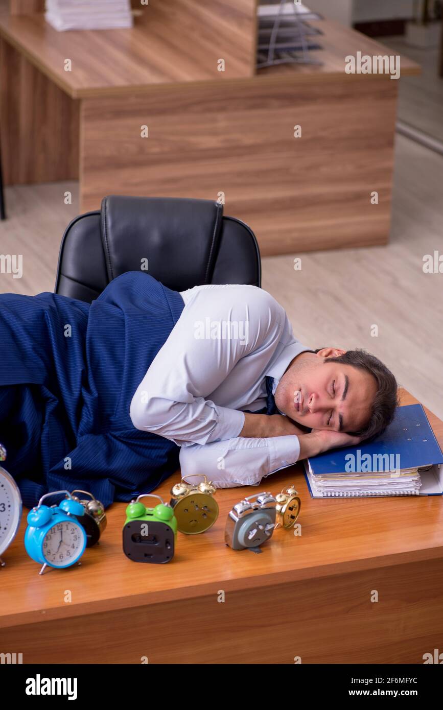 Young businessman sleeping in the office in time management concept ...