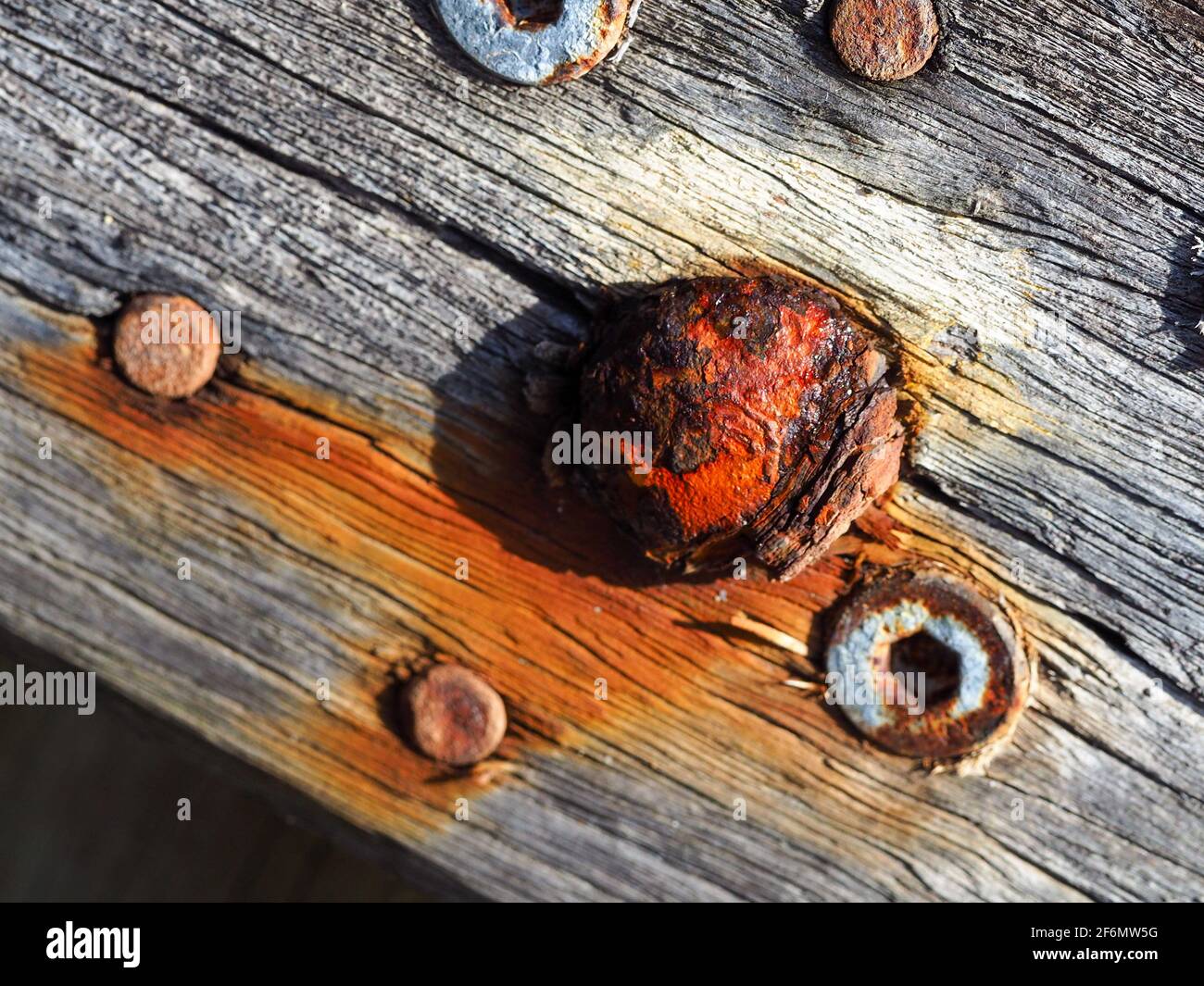 a rusty bolt in some weather beaten wood on a staircase railing outside ...