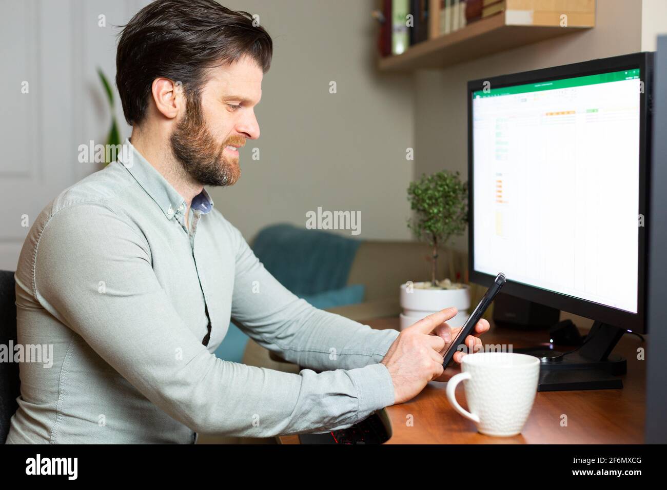 Man taking video call on his cell phone working from home on desktop ...