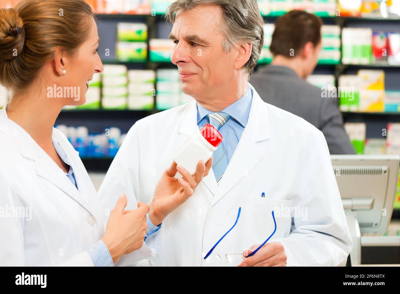 Two pharmacists with pharmaceuticals in hand consulting each other in a ...
