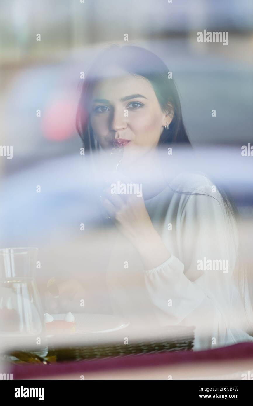 View through the window of cafe at young woman sitting inside and ...