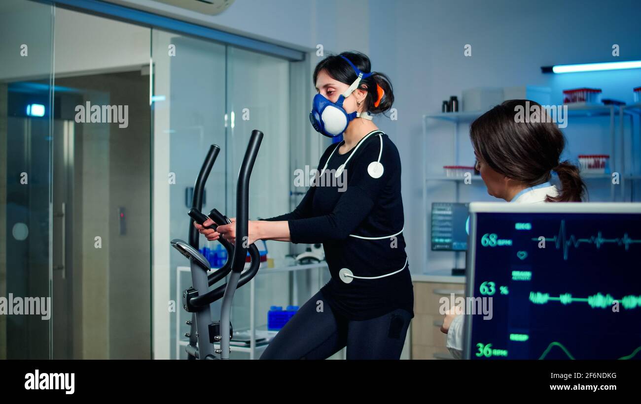 Woman athlete with mask running on cross trainer after medical ...