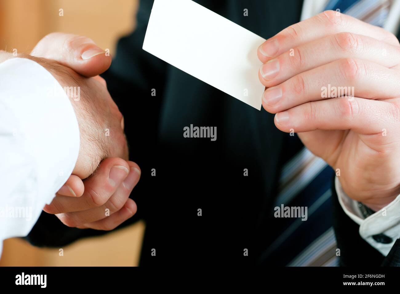 Businessmen having handshake, one handing business card over; only ...