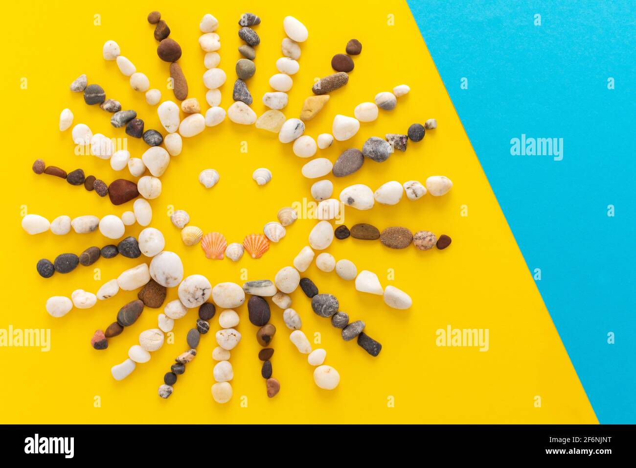 Abstract smiling sun from sea pebbles and seashells on yellow and blue ...