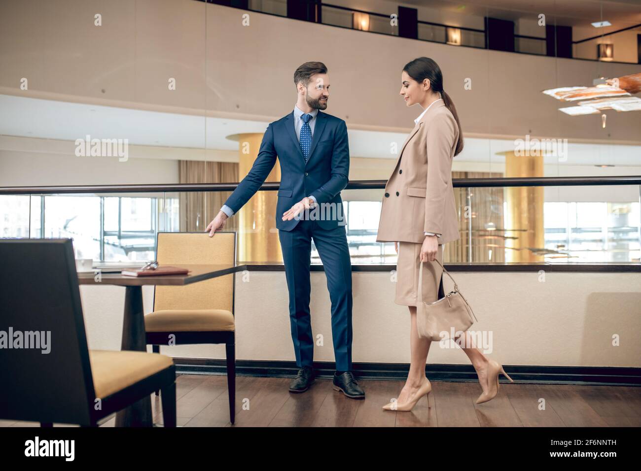 Polite man. Man in a blue suit inviting a woman to sit Stock Photo - Alamy